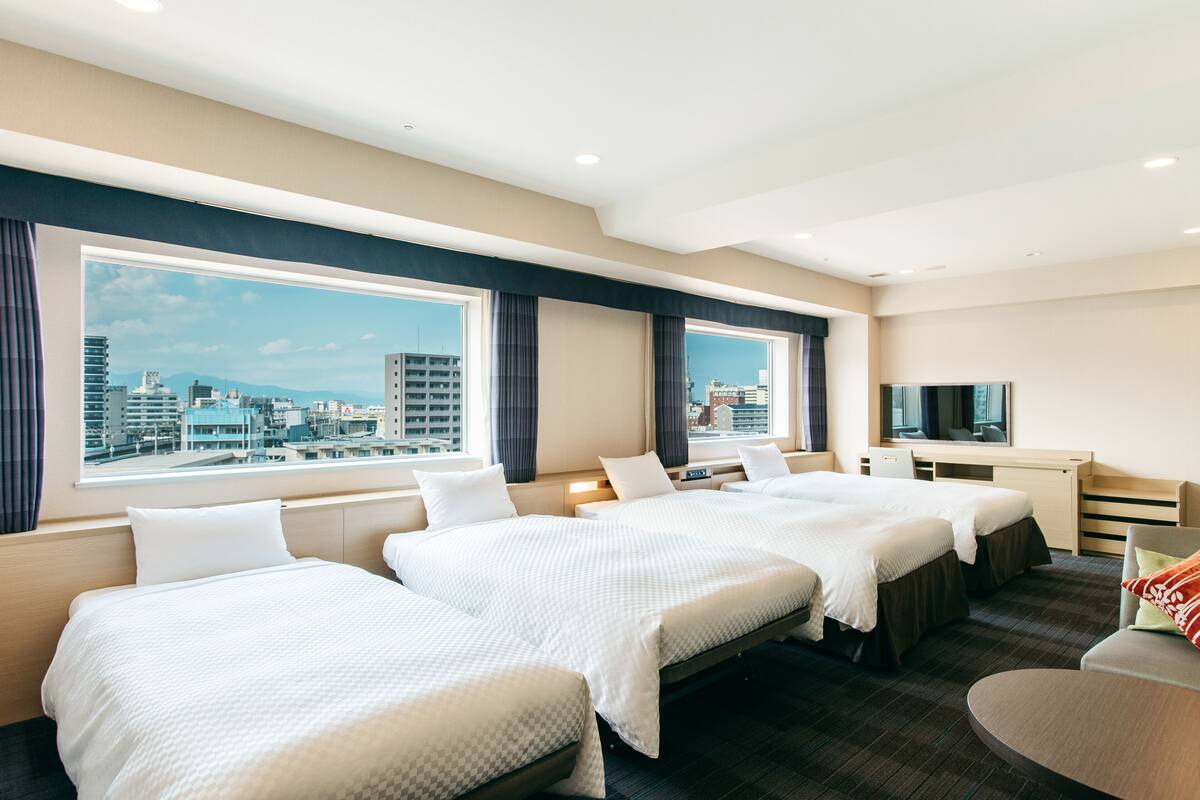 Quarto de hotel com duas camas, uma escrivaninha, televisão e vista para a paisagem urbana.