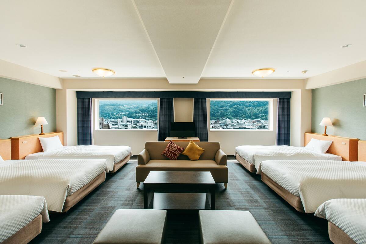 Quarto de hotel com duas camas, um sofá, uma mesa e uma televisão.