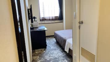 Quarto de hotel com uma cama, escrivaninha, janela com cortinas e radiador.