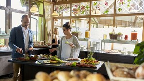 Disposição de buffet com diversos alimentos e um homem e uma mulher servindo.