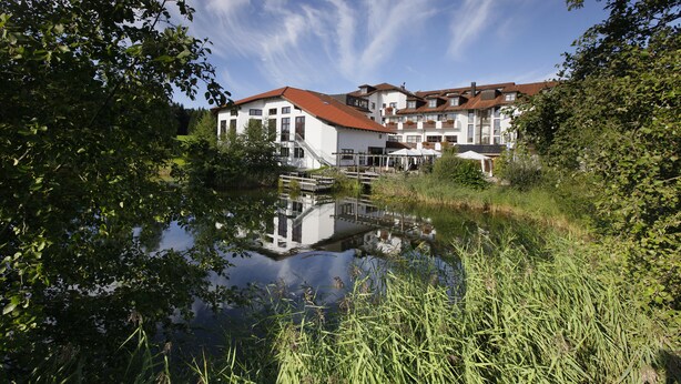 Um hotel na beira do lago, com seu reflexo na água, cercado por vegetação.