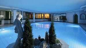 Piscina interior moderna com uma estátua, parede de vidro e chão revestido com azulejos.