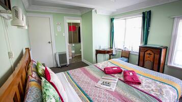 Quarto com cama, cômoda, cadeira, janela com cortinas e porta que dá para um banheiro.