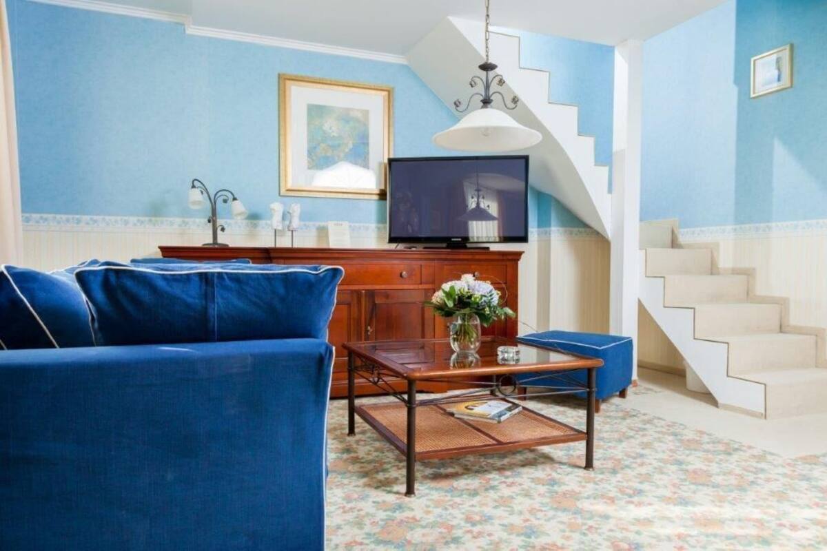 Uma sala de estar com um sofá azul, uma mesa de centro de madeira, uma televisão e uma escada.