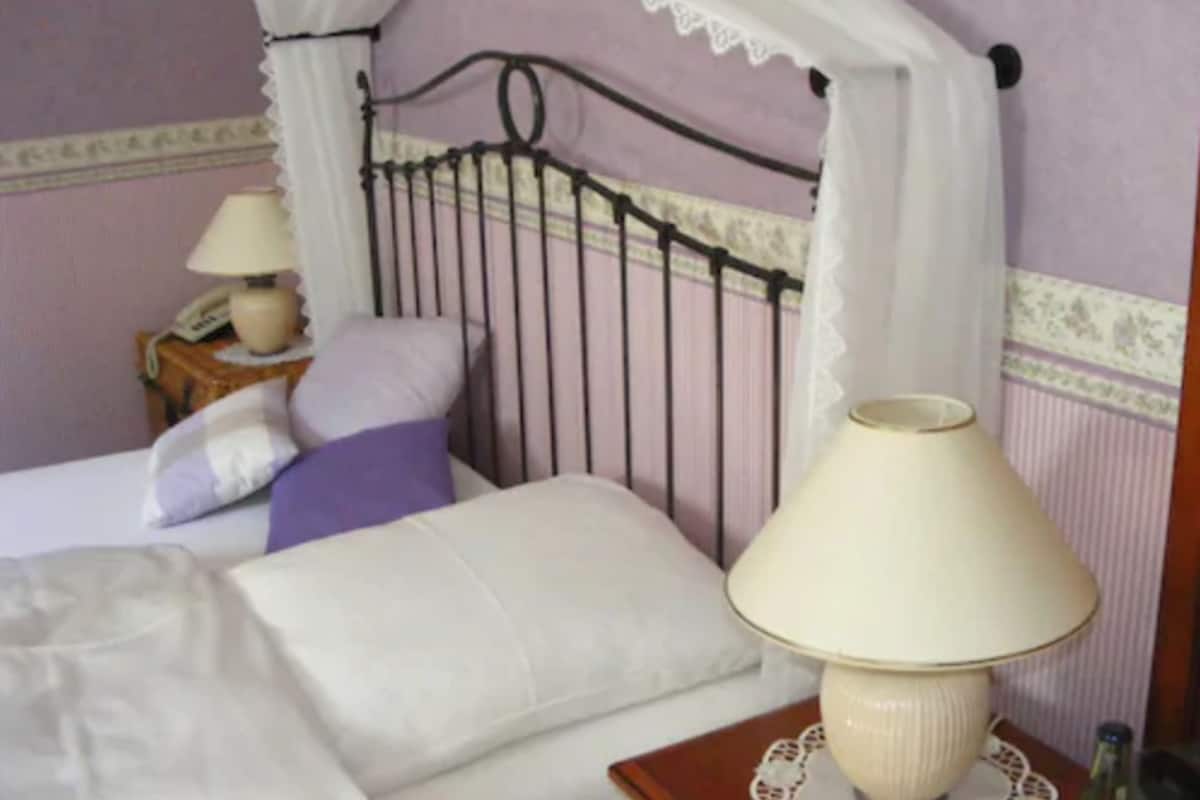 Quarto com cama, mesa de cabeceira com abajur e cabeceira decorativa.