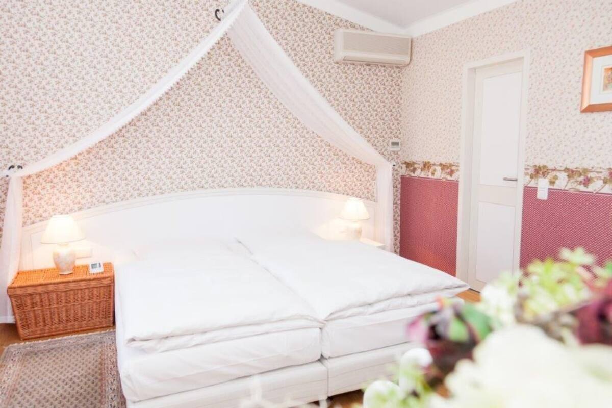 Quarto com cama de dossel, mesa de cabeceira com luminária e ar-condicionado fixado na parede.