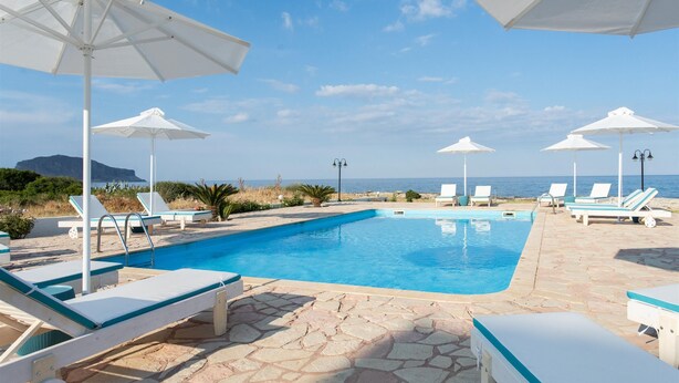 Área da piscina com espreguiçadeiras e guarda-sóis, céu claro e vista para o mar.