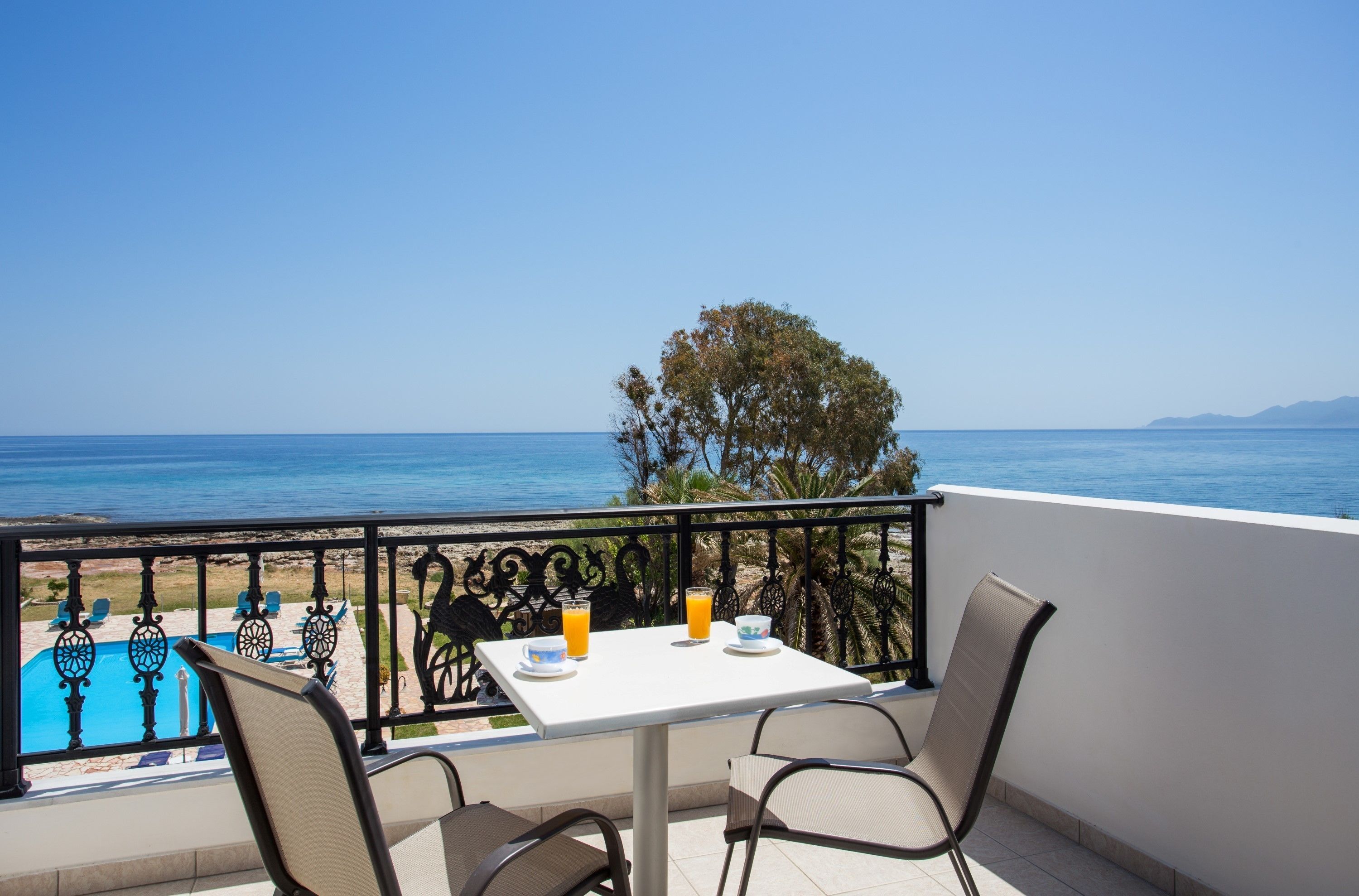 Varanda com mesa e cadeiras, vista para uma piscina e para o mar.