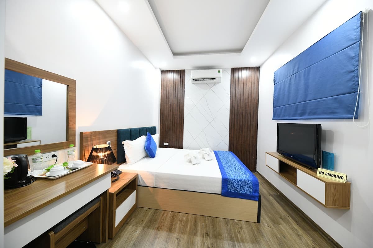Quarto de hotel moderno com cama, mesa de cabeceira, televisão e aviso de 'Proibido Fumar'.
