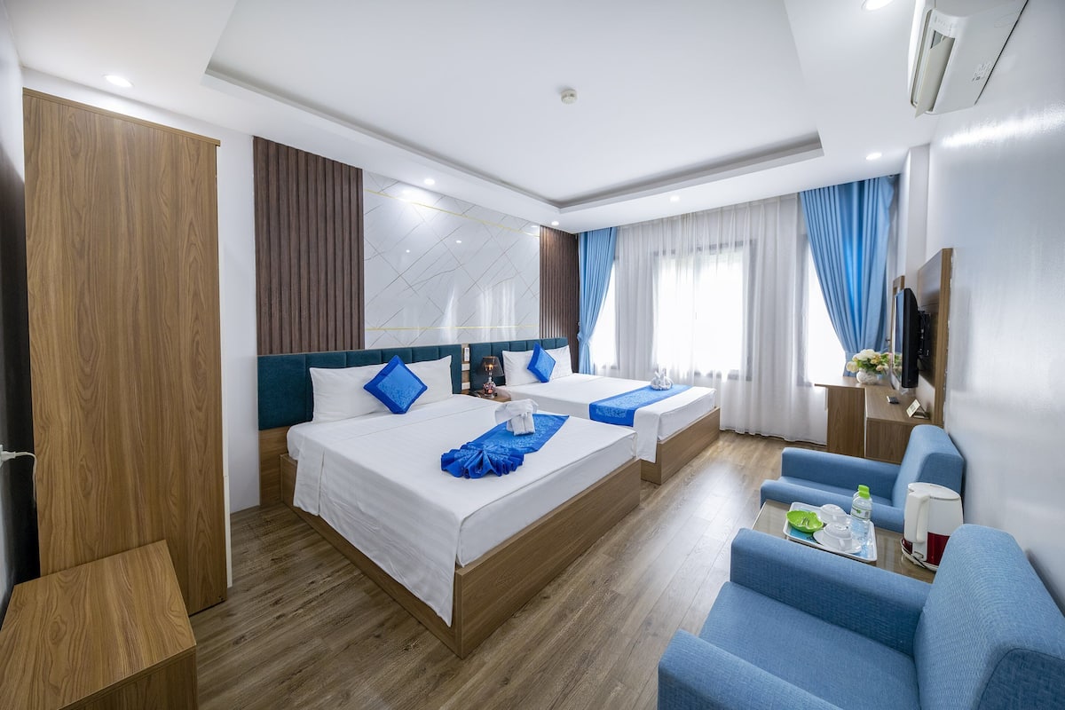 Quarto de hotel com duas camas, um sofá, uma mesinha com bandeja e uma televisão.