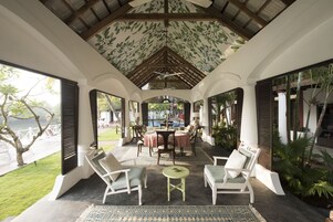 Uma área de estar coberta ao ar livre, com mesa e cadeiras, cercada por janelas amplas e vista para uma piscina e jardim.