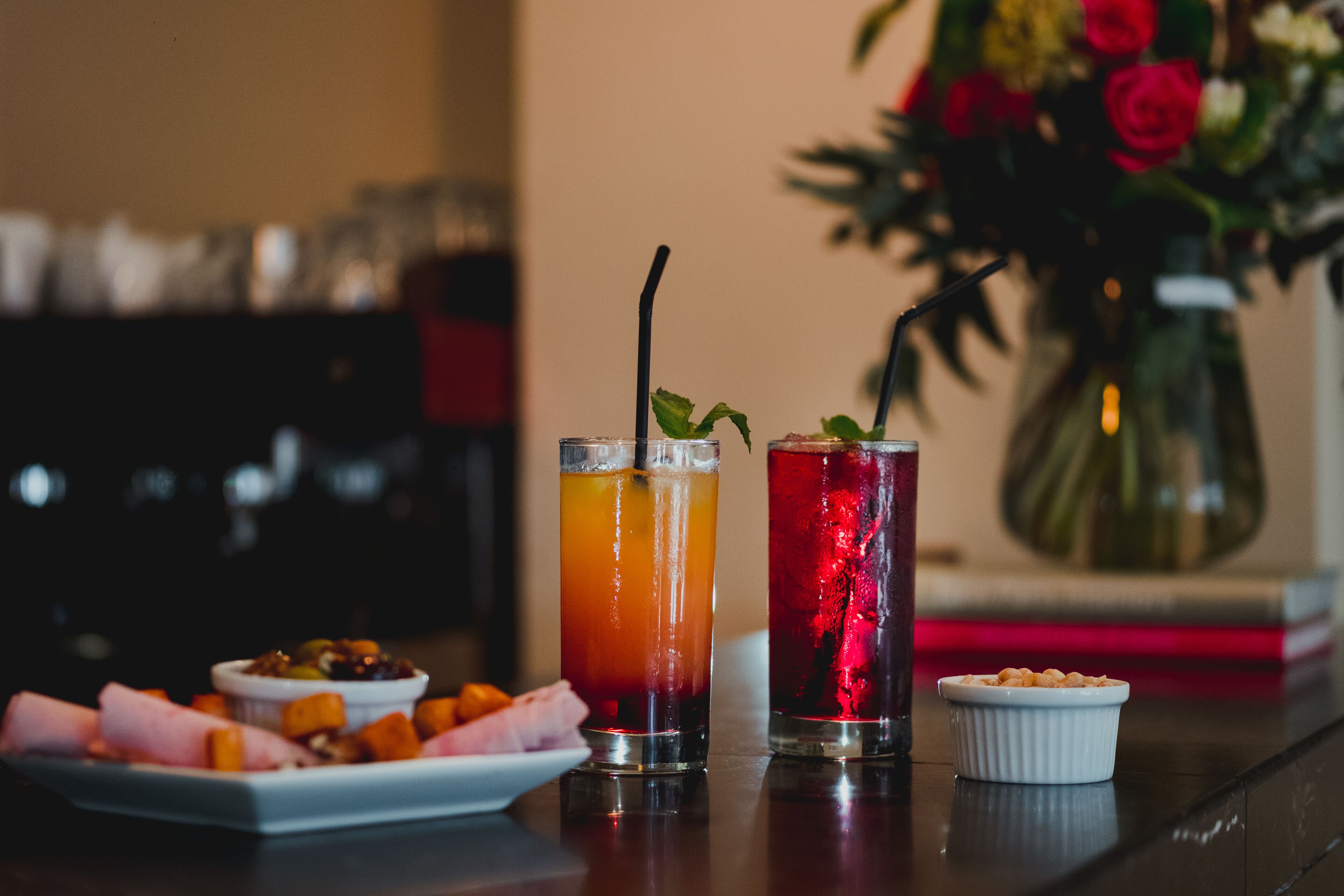 Uma mesa com duas bebidas, um pequeno prato de nozes e um prato de comida.