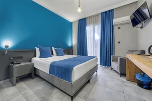 Quarto de hotel moderno com cama, mesa de cabeceira, escrivaninha e televisão.