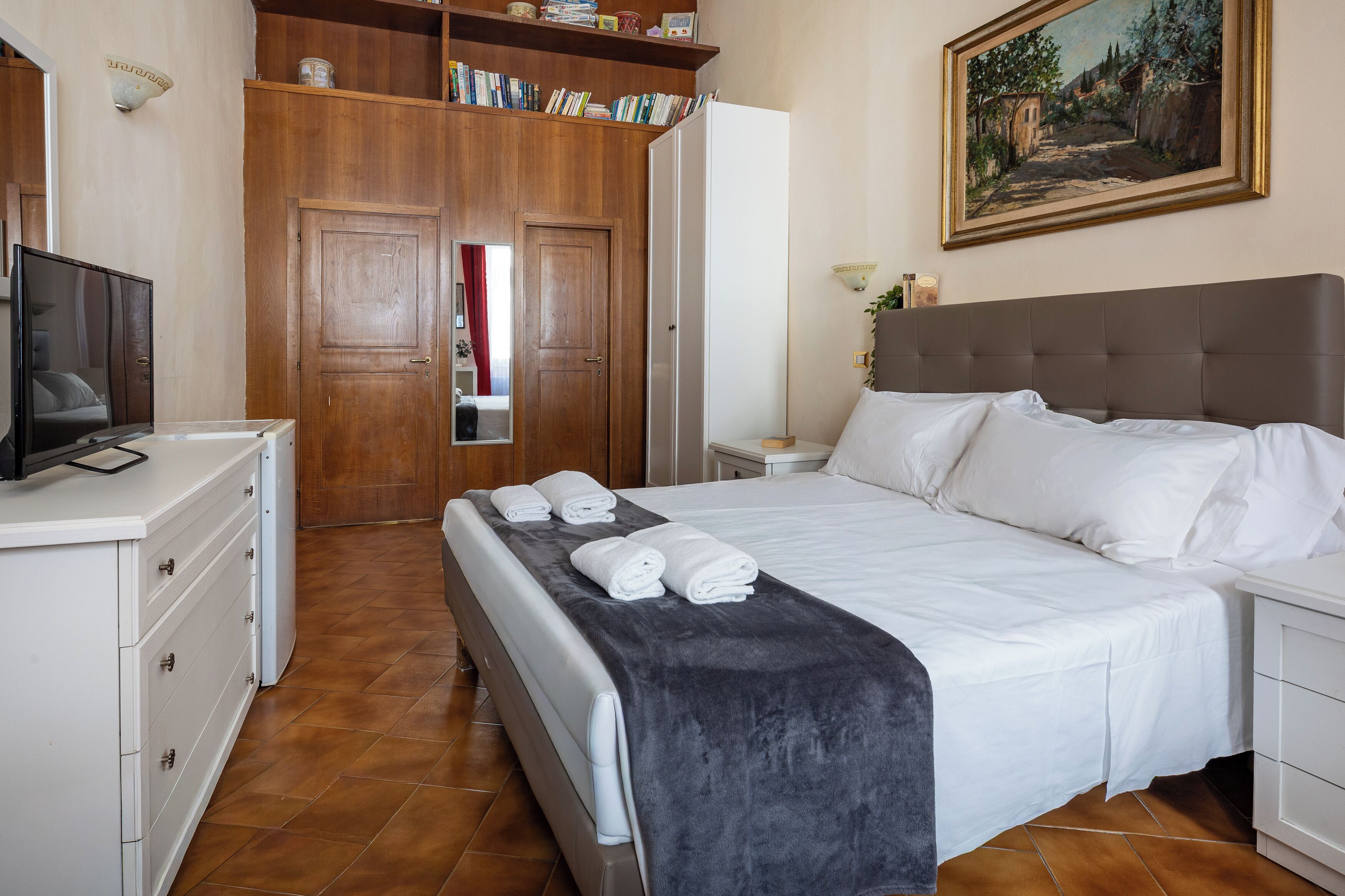 Quarto de hotel com cama, televisão, guarda-roupa e um quadro na parede.