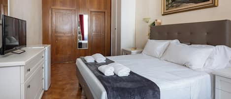 Quarto de hotel com cama, televisão, guarda-roupa e um quadro na parede.