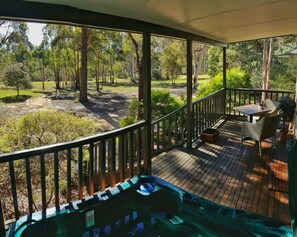 Uma área externa coberta com hidromassagem, deck de madeira e vista para uma paisagem arborizada.