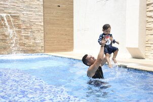 Um homem levanta uma criança acima de uma piscina, com água espalhando ao redor.