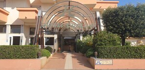 Entrada de hotel com um arco de metal, um caminho que leva à entrada e sebes bem cuidadas.