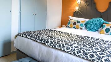 Quarto de hotel com uma cama, uma luminária de cabeceira e uma revista no banquinho.