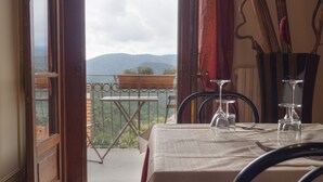 Uma sala de jantar com uma mesa posta para dois, vista das montanhas pela porta da varanda e um vaso de planta na varanda.