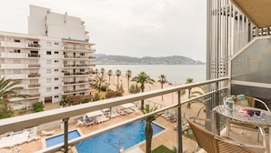 Uma varanda com piscina, espreguiçadeiras e vista para o mar e edifícios.