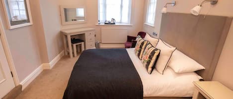 Quarto com cama, mesa de cabeceira, escrivaninha, cadeira e janela com cortinas.