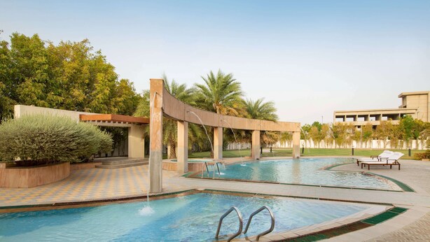 Área de piscina com duas piscinas, palmeiras e um deque coberto.
