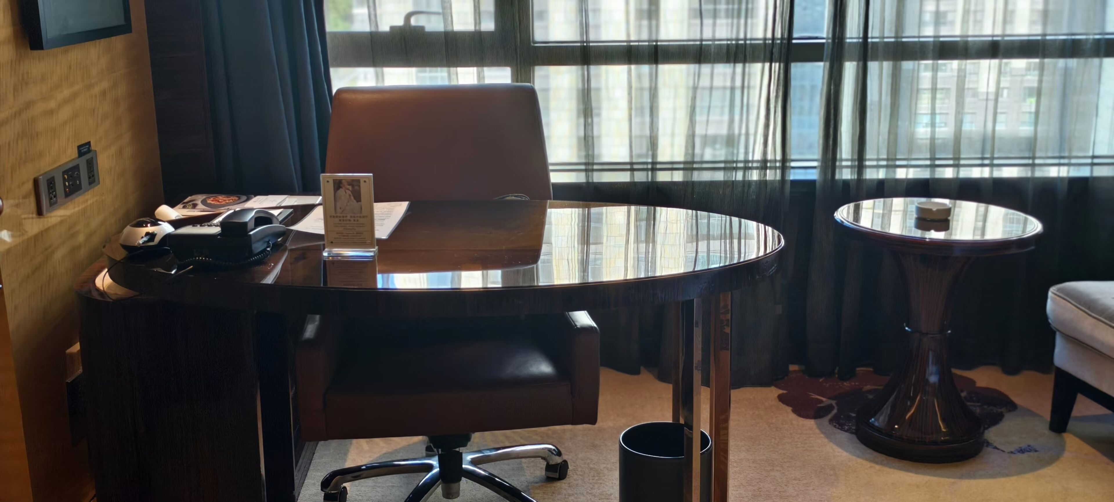 Um espaço de escritório moderno com uma mesa de vidro, uma poltrona de couro e uma pequena mesa redonda.