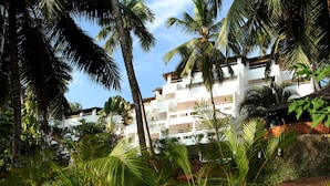 Resort com edifício branco, palmeiras e jardins em terraços.
