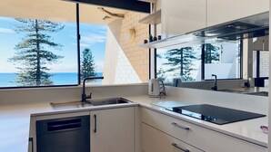Uma cozinha moderna com lava-louças, pia e janela com vista para uma árvore e um edifício.