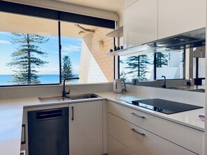 Uma cozinha moderna com lava-louças, pia e janela com vista para uma árvore e um edifício.