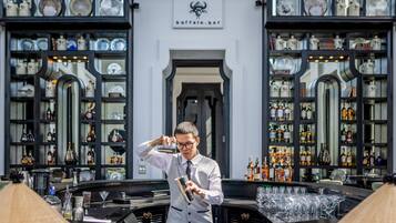 Um bartender em um bar, com prateleiras cheias de garrafas e copos atrás dele.