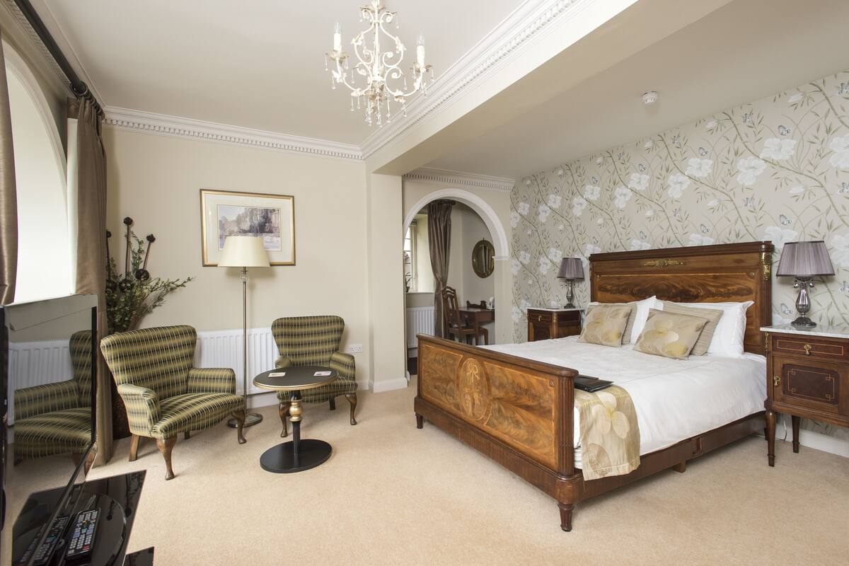 Quarto com uma cama grande, uma cadeira, uma mesinha e um candelabro.