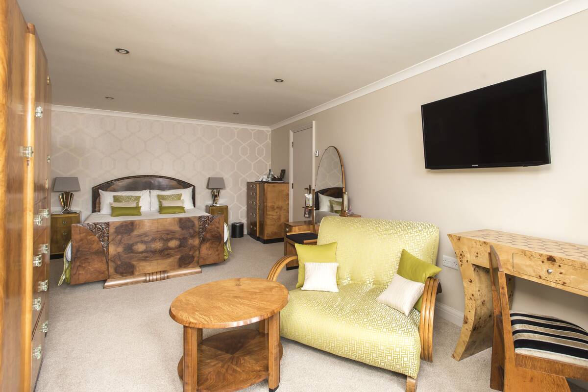 Quarto de hotel com cama, sofá, mesa de madeira e TV fixada na parede.