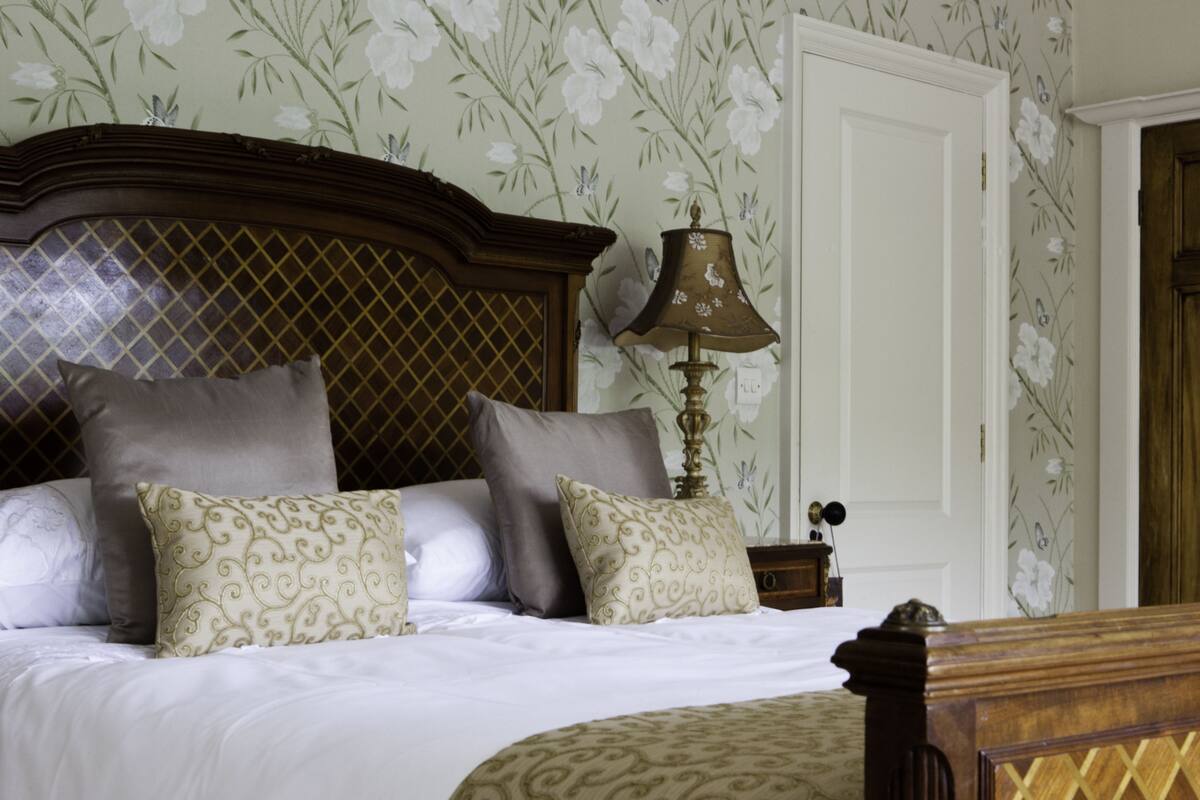 Uma cama bem arrumada com almofadas estampadas, cabeceira de madeira e luminária de cabeceira.