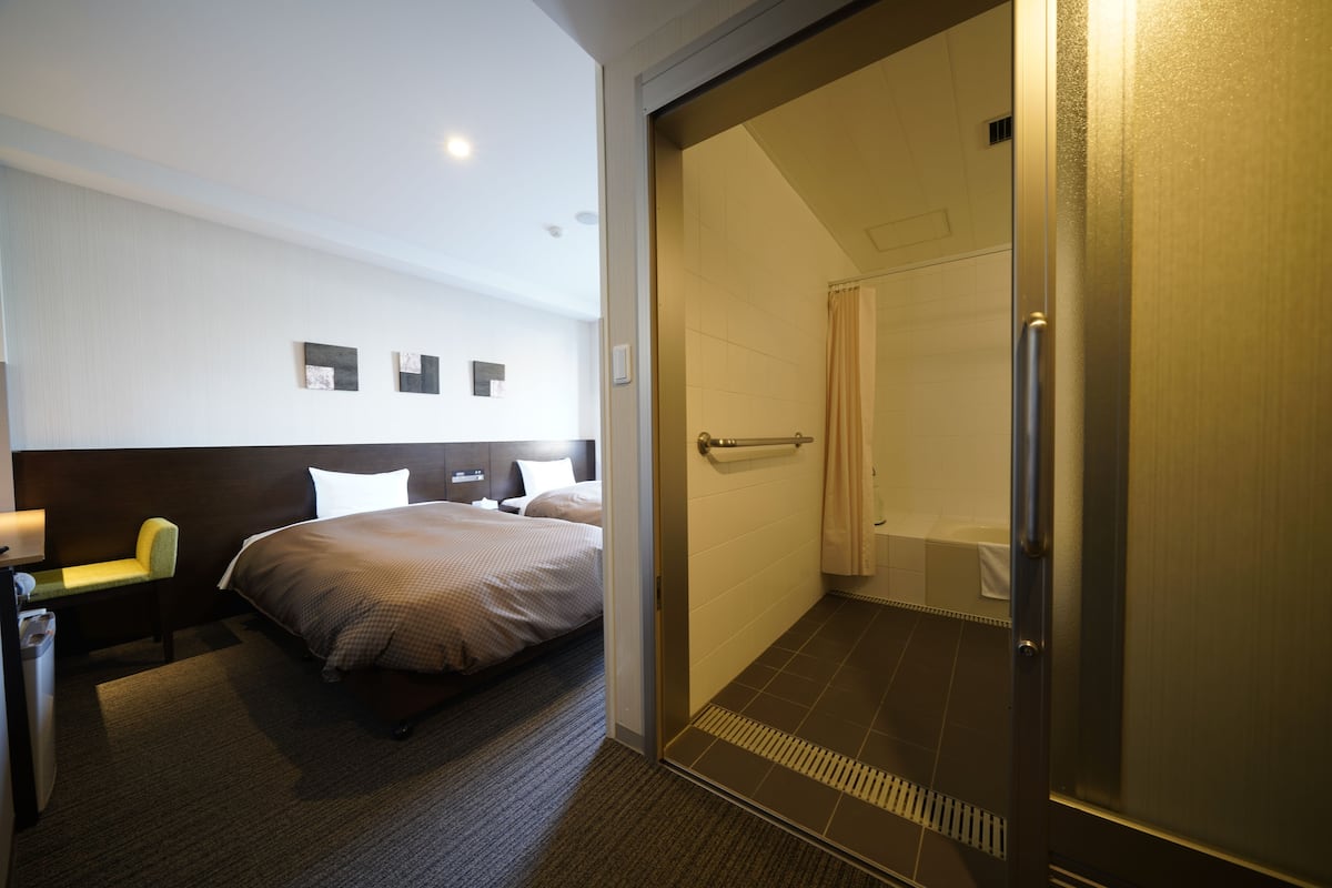 Quarto de hotel com cama, escrivaninha e área de chuveiro.