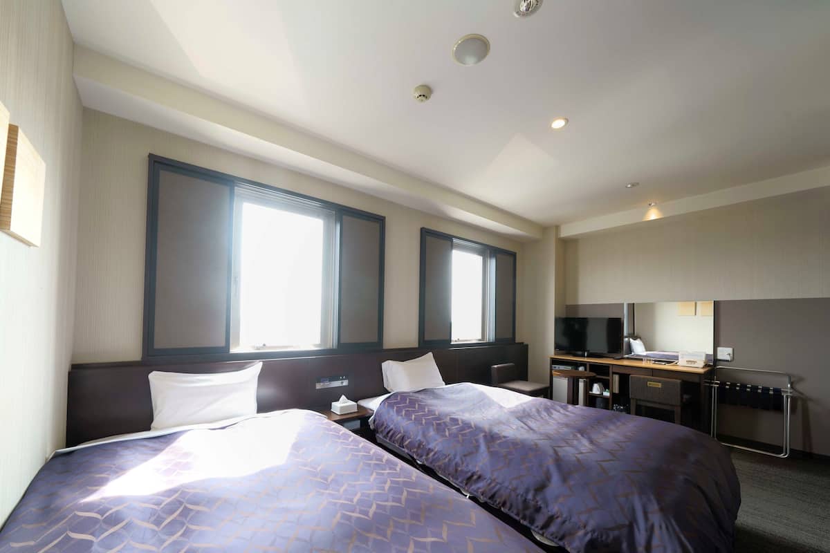 Quarto de hotel com duas camas, uma mesa, uma televisão e uma janela.