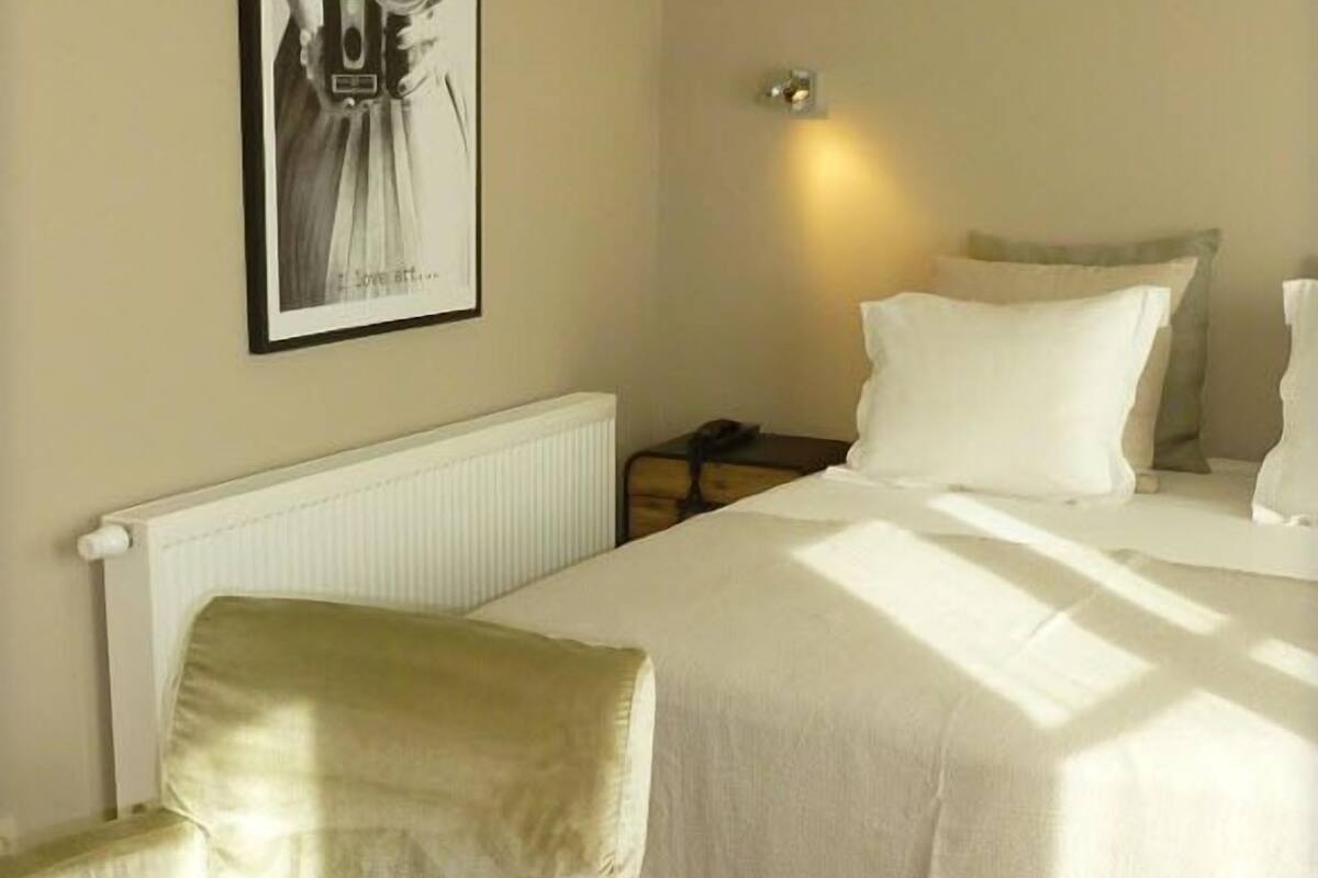 Quarto de hotel com cama, cadeira, mesa com uma xícara e quadro pendurado na parede.