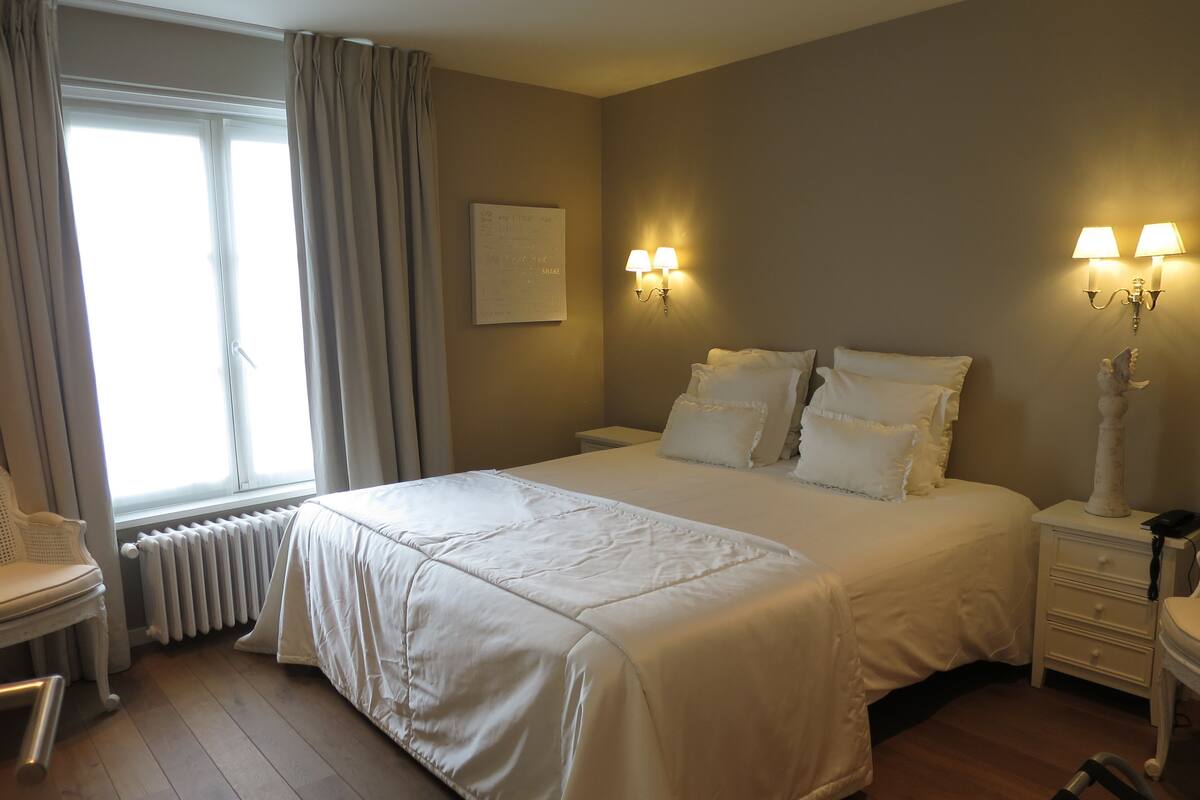 Quarto bem arrumado com uma cama grande, luminárias de cabeceira, um radiador e uma cadeira.