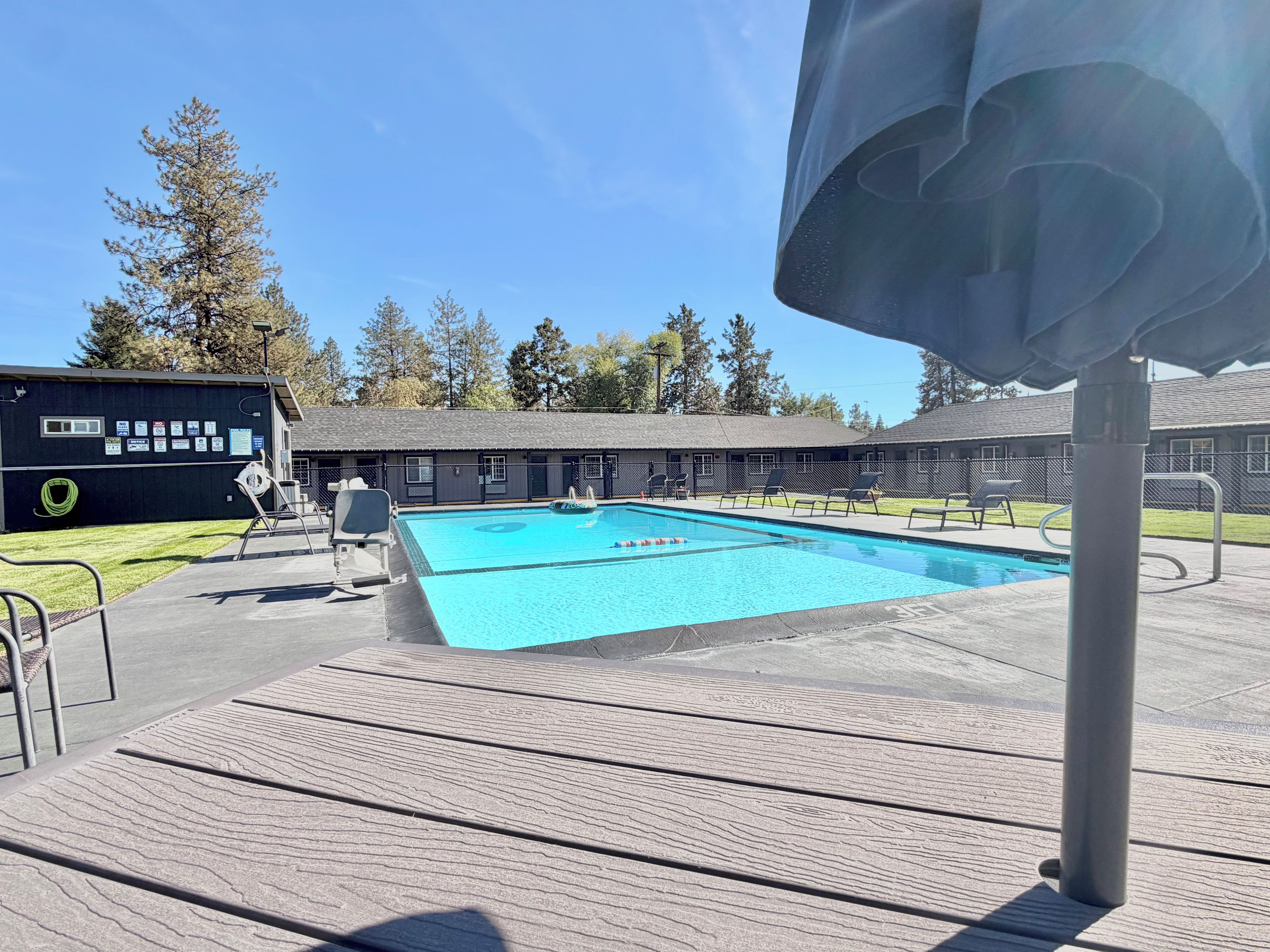 Piscina com deck de madeira, espreguiçadeiras e um edifício com fachada escura ao fundo.
