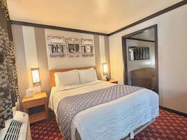 Quarto de hotel com cama, abajures, ar condicionado fixado na parede e quadros com imagens de marcas de luxo.