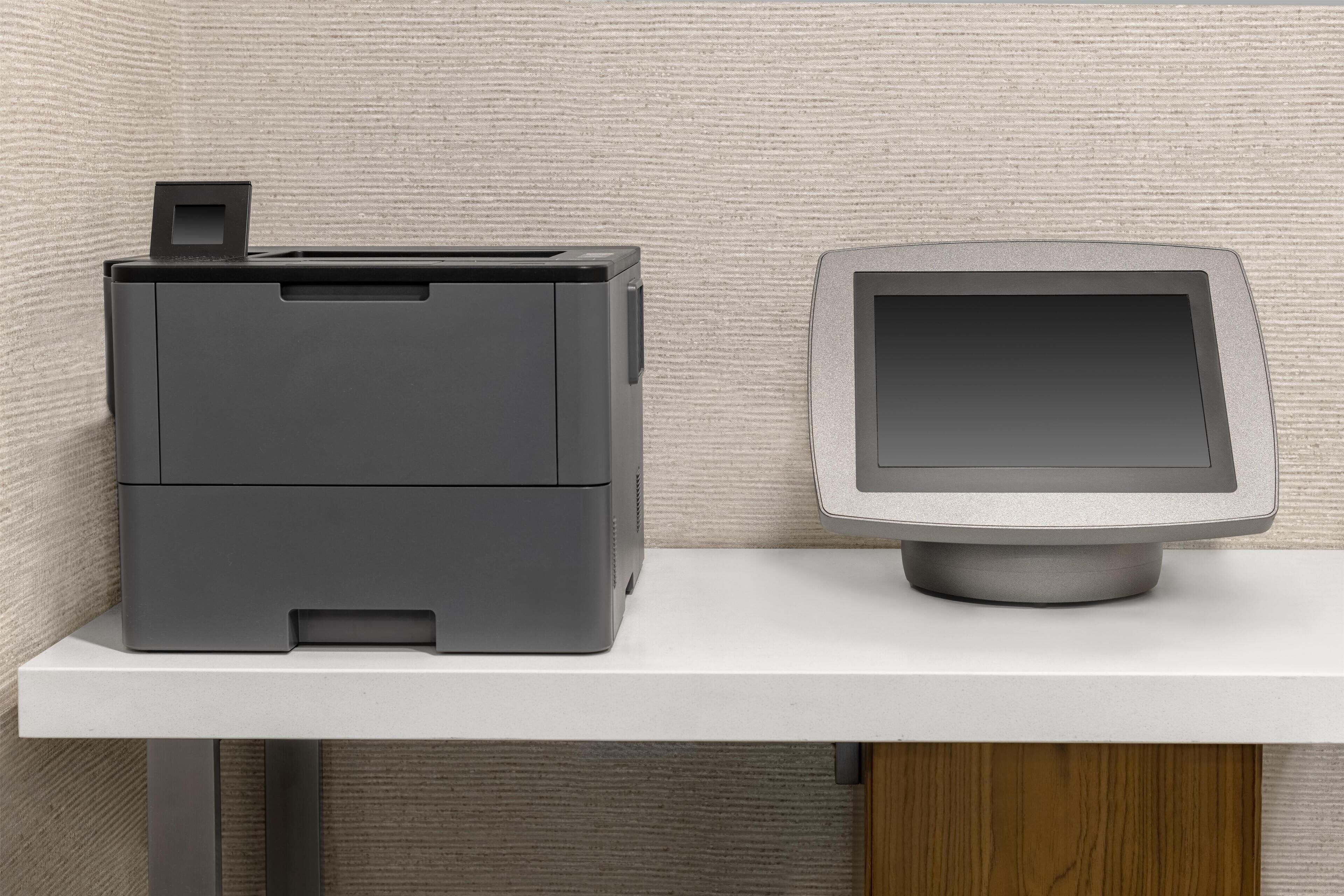 Impressora e monitor sobre uma mesa branca, com um fundo de parede texturizado.