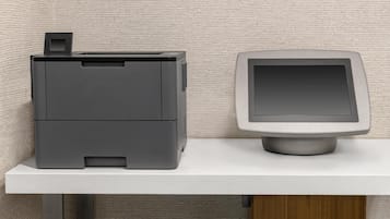 Impressora e monitor sobre uma mesa branca, com um fundo de parede texturizado.