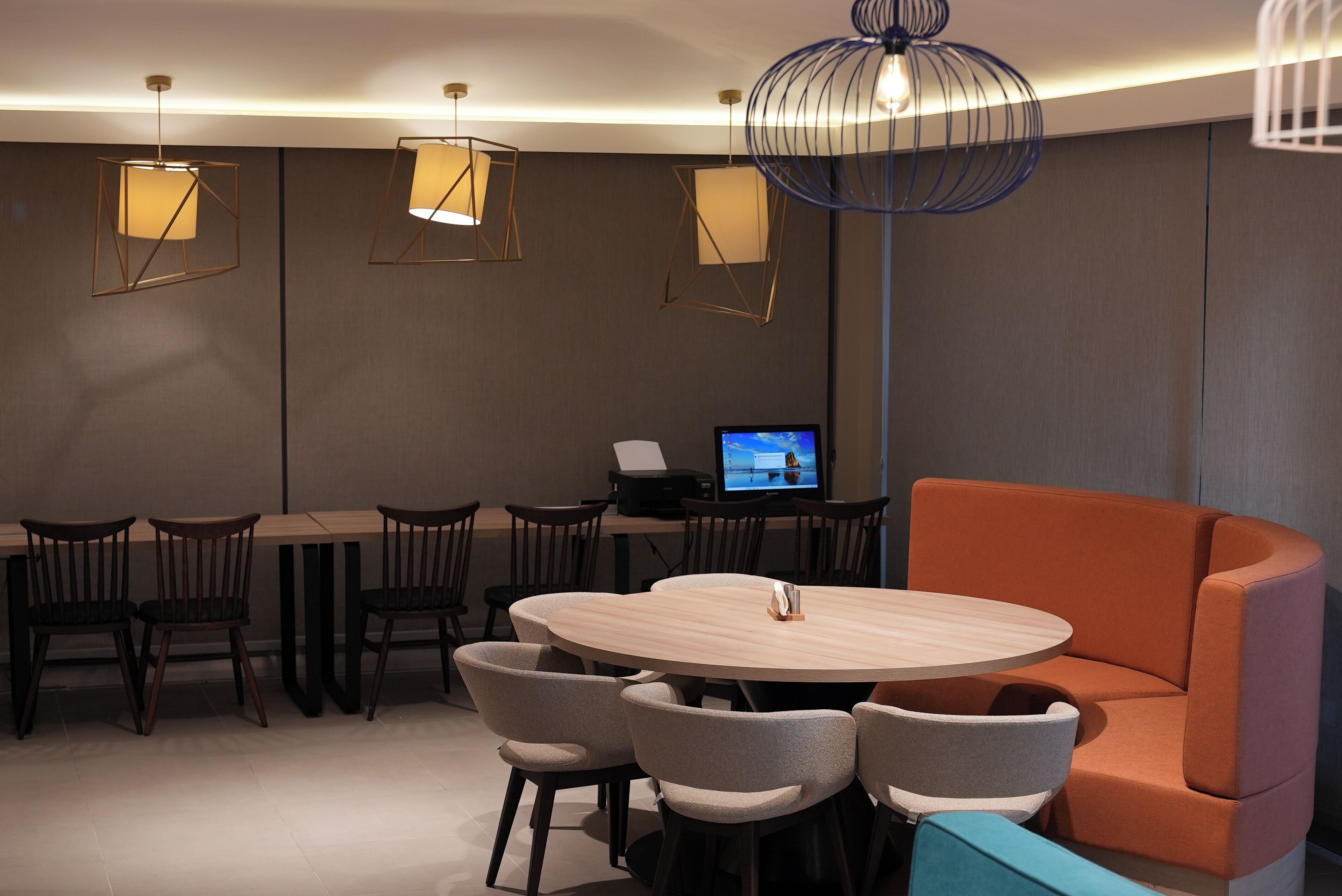 Uma sala de conferências moderna com uma mesa redonda, seis cadeiras, um laptop em uma mesa e um sofá laranja grande.