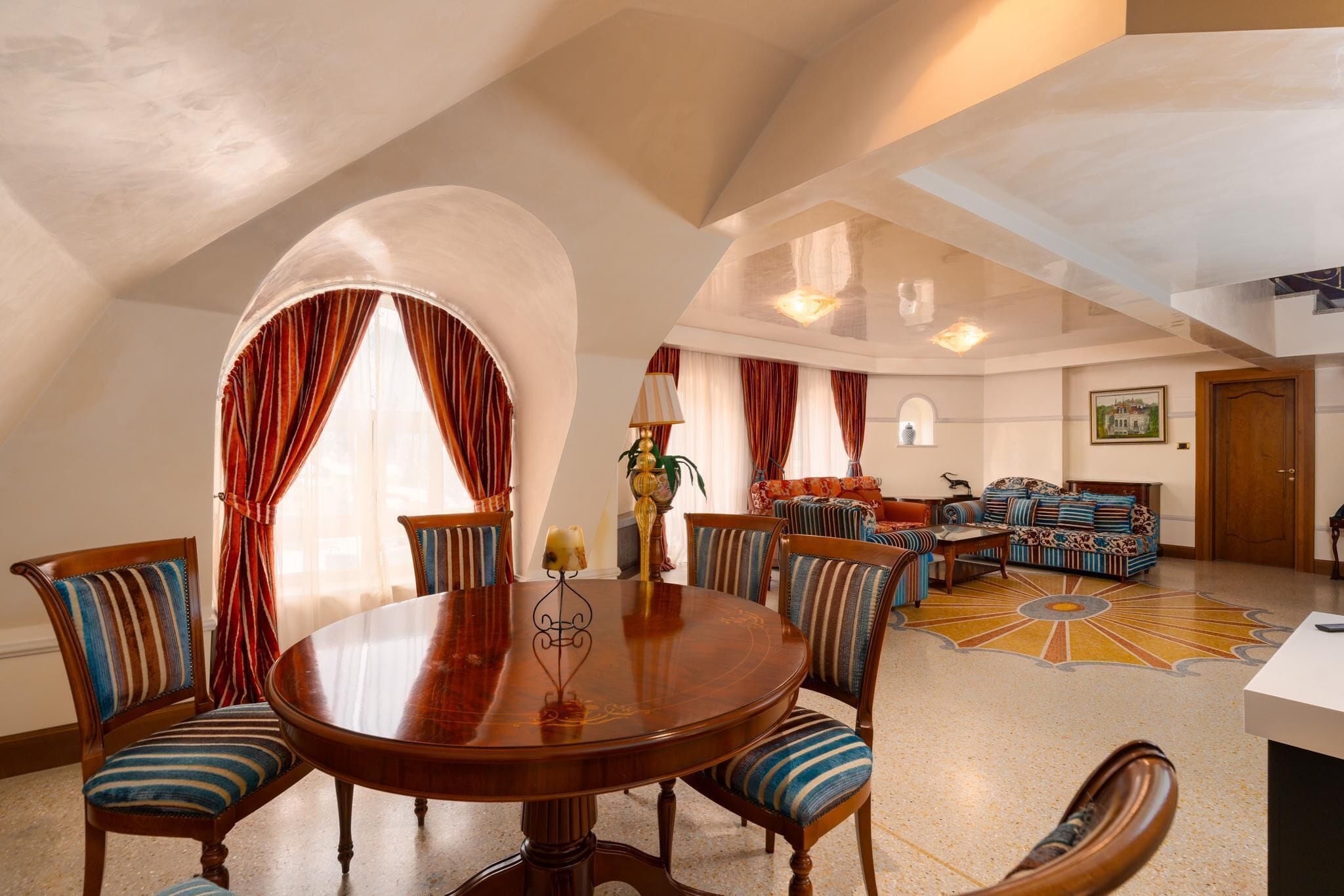 Uma sala de jantar com uma mesa redonda de madeira, cadeiras estofadas listradas e um chão estampado.