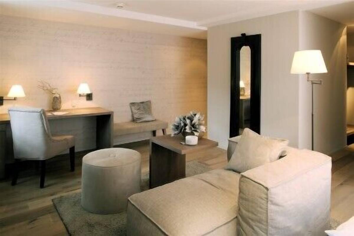 Uma sala de estar moderna com sofá, banqueta e uma mesinha com abajur.