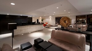 Um lobby moderno com balcão de recepção, área de estar e uma grande peça decorativa na parede.