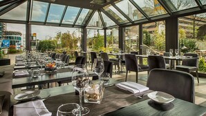 Restaurante com mesas ao ar livre, grandes janelas e vista para a cidade.