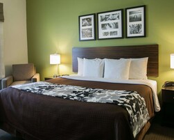 Quarto de hotel com uma cama grande, duas mesas de cabeceira, uma cadeira e três quadros na parede.