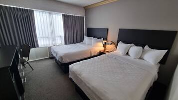 Quarto de hotel com duas camas, uma escrivaninha e uma cadeira.